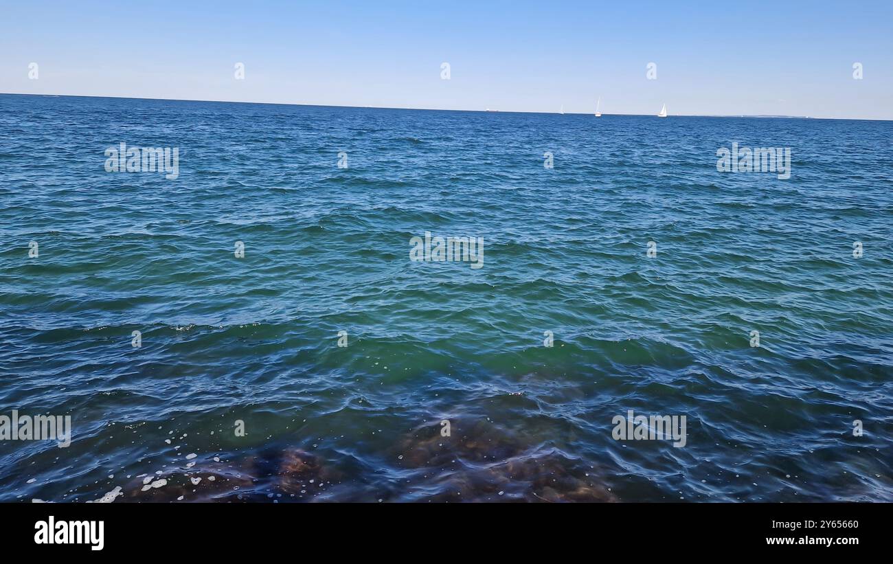 Serene ocean waves with sailboats in the distance under a clear sky ...
