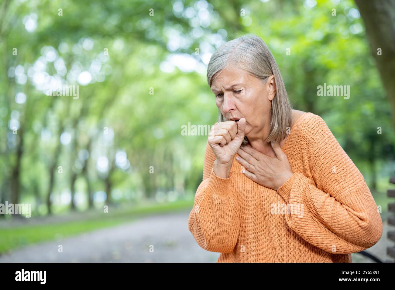 Elderly woman coughing in outdoor park setting showing discomfort ...