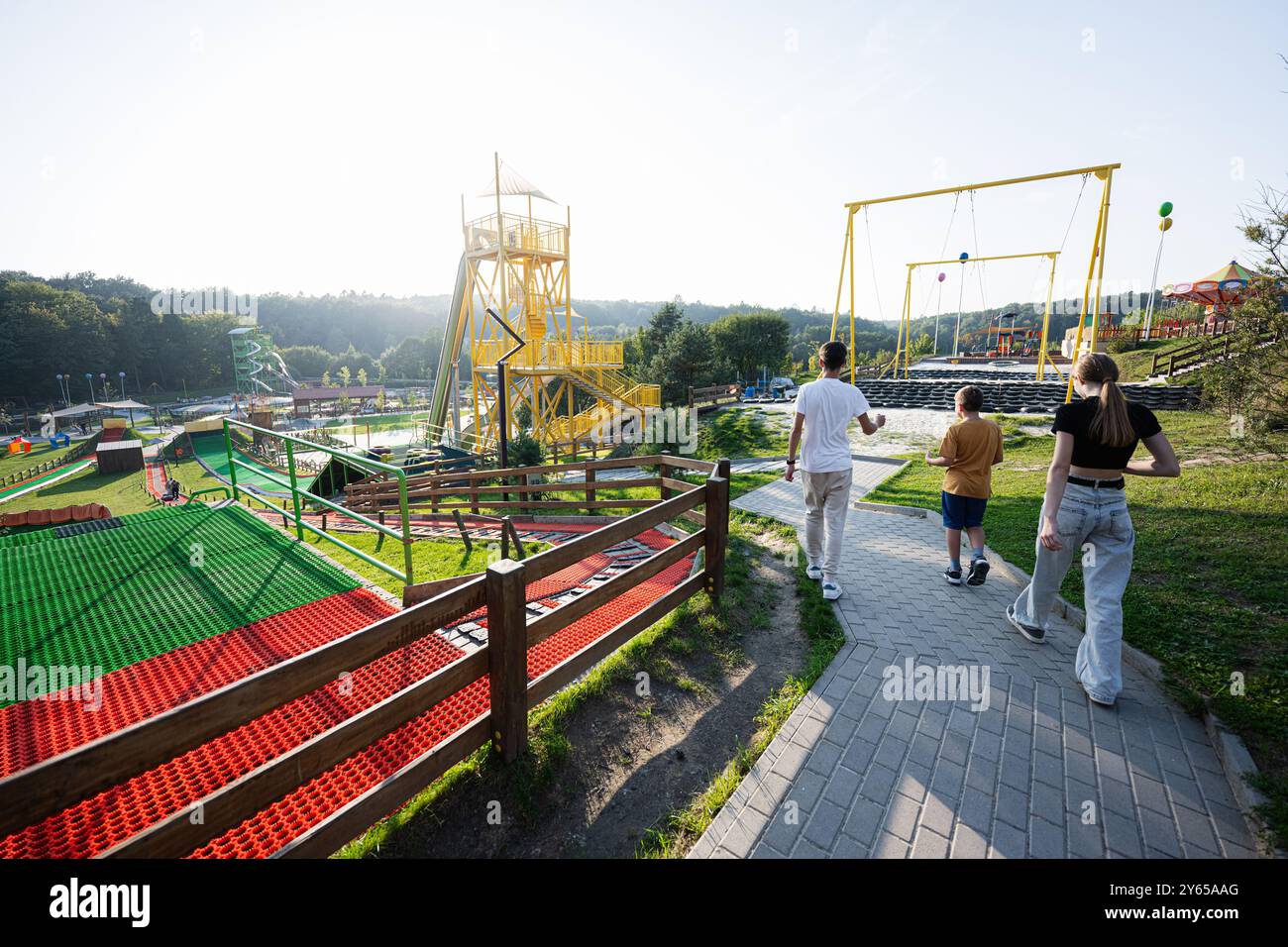 Teens walks through a vibrant amusement park on a sunny day, enjoying ...