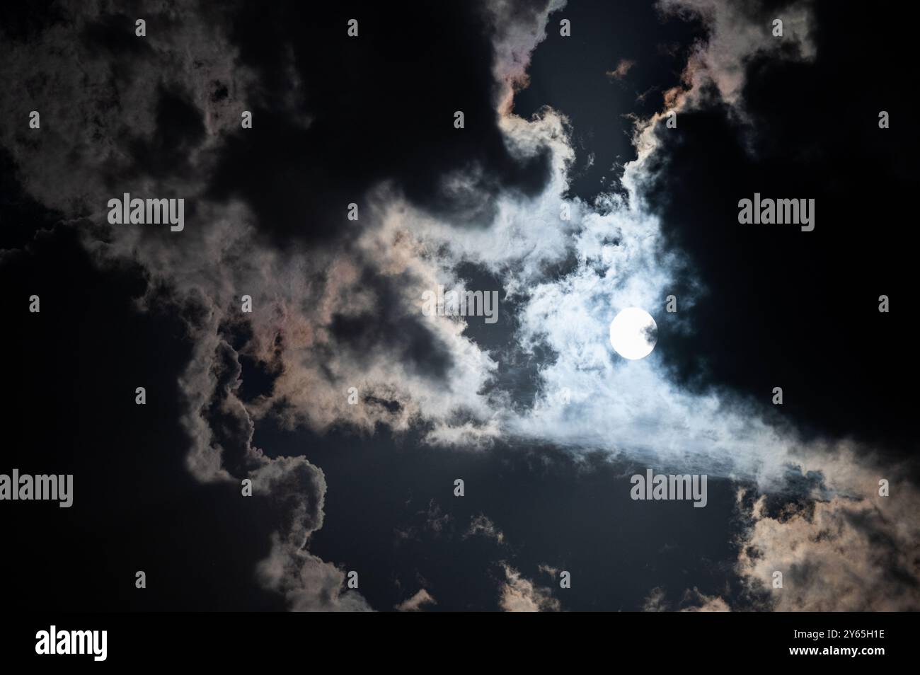 A dramatic night sky with the moon partially obscured by dark clouds ...