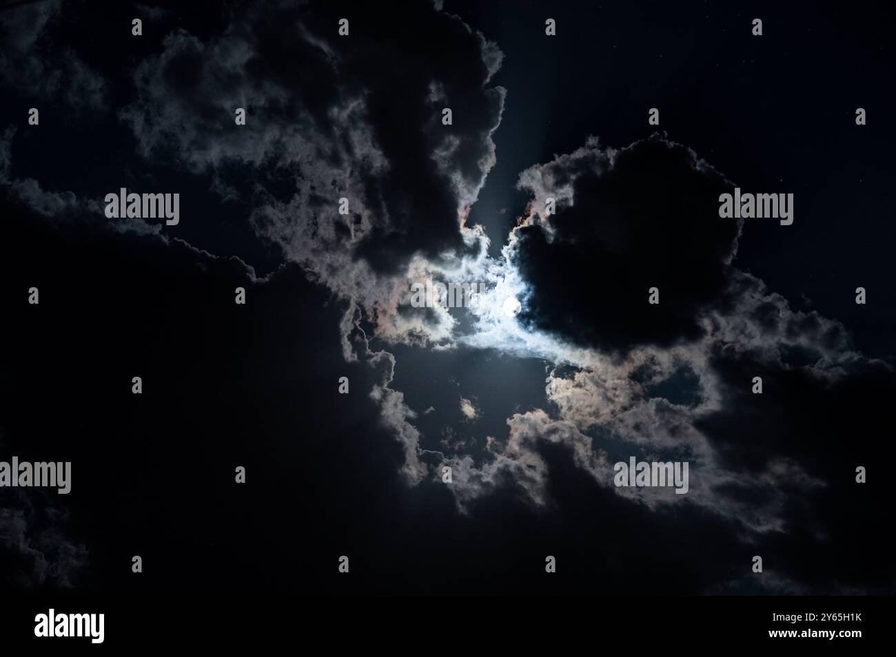 A dramatic night sky with the moon partially obscured by dark clouds ...