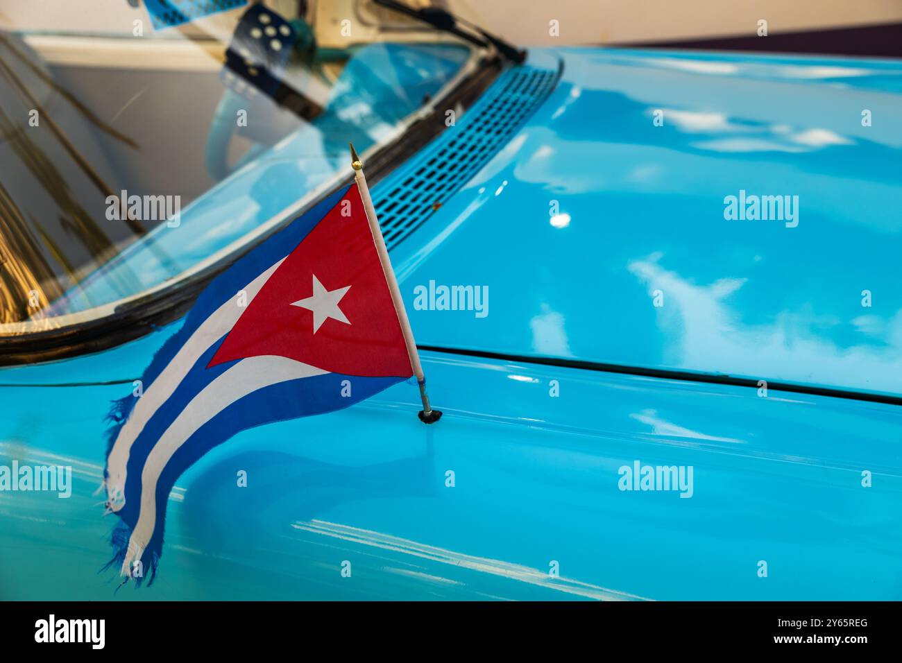 A worn Cuban flag displayed on the hood of a glossy turquoise vintage ...