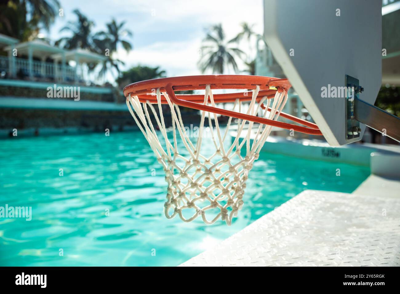 A basketball hoop over a vibrant turquoise pool with a backdrop of lush ...