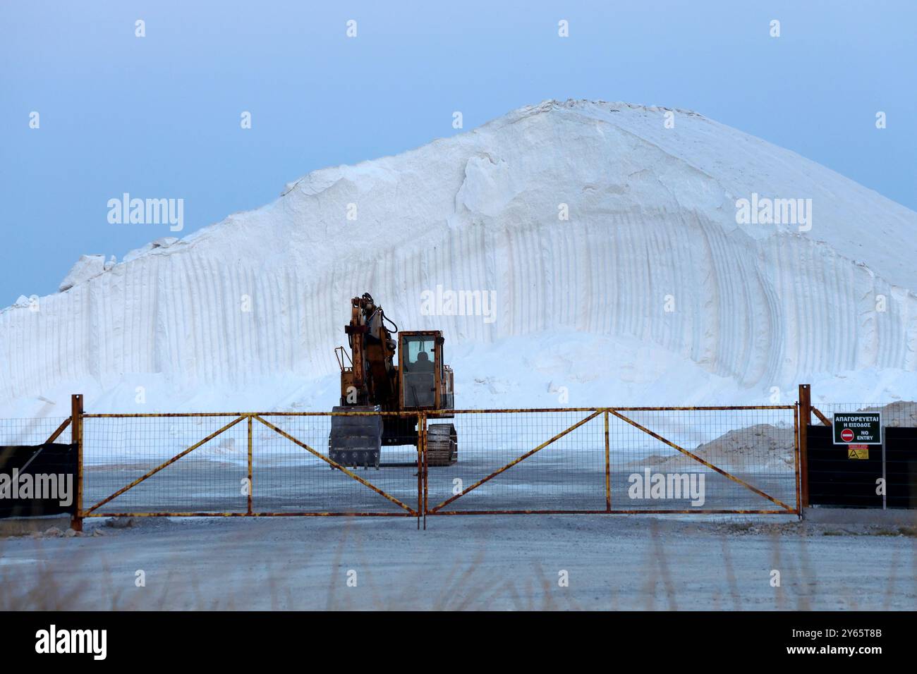 A large pile of salt with an excavator in front of a closed gate at a ...