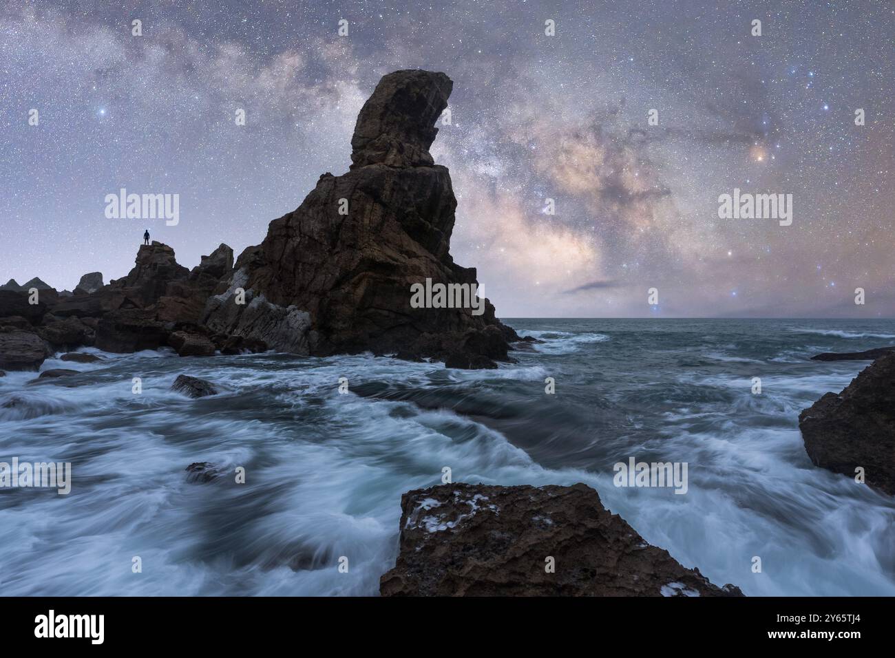 Dramatic landscape showing the Milky Way spread over tumultuous waves of the sea breaking ...