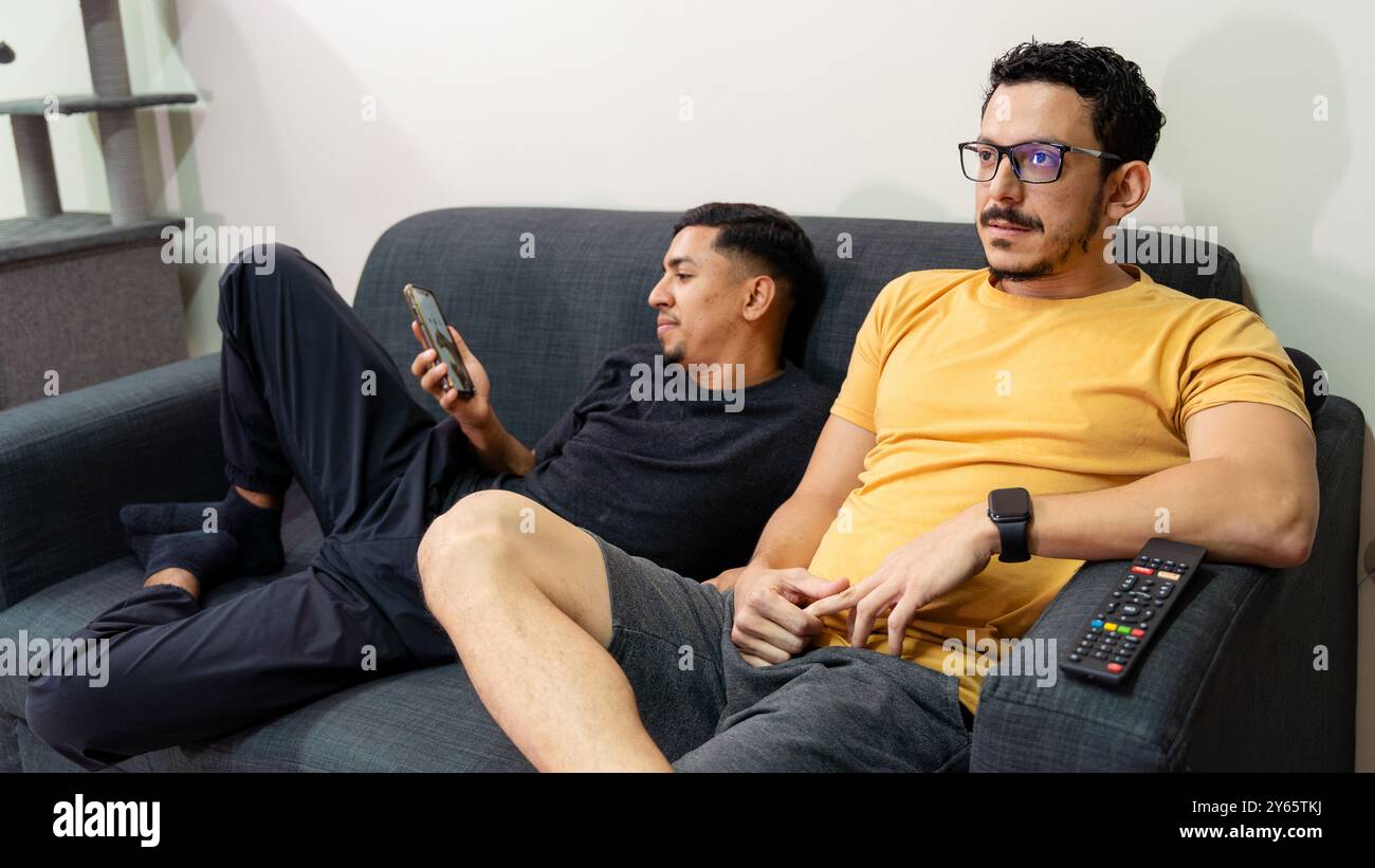 A gay couple enjoys a cozy moment on the couch, with one man browsing ...