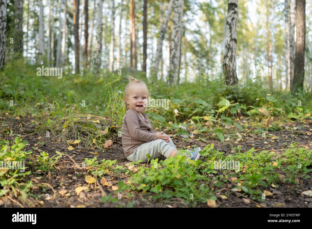 A happy toddler sits on the forest ground, surrounded by lush greenery ...