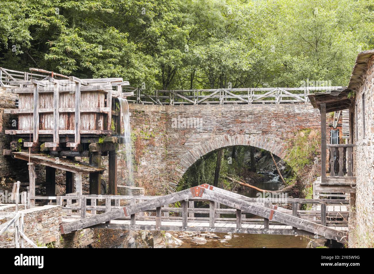 An old wooden water mill operates next to a brick arch bridge ...