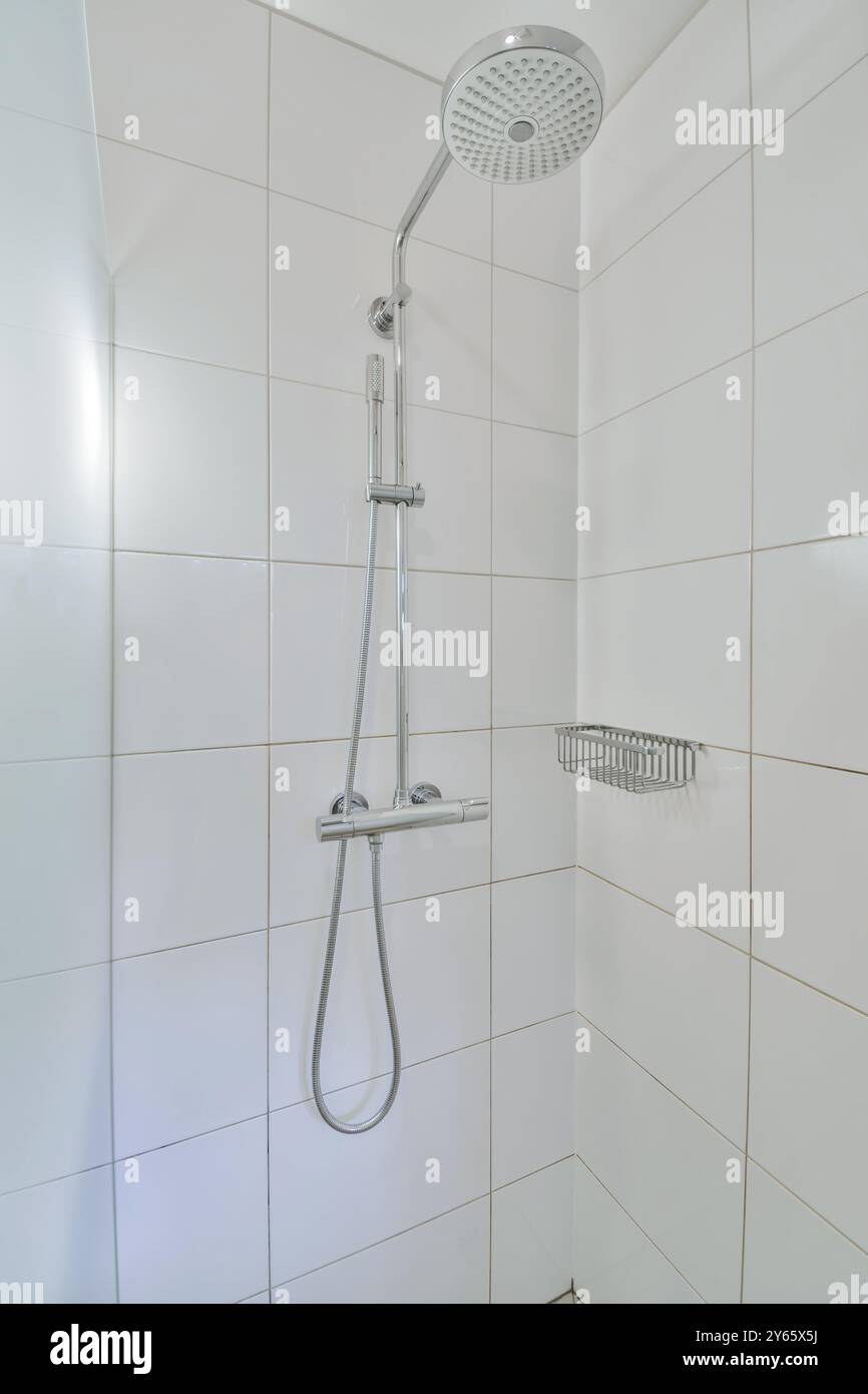 A sleek, modern shower head and fixture mounted on glossy white tiles ...