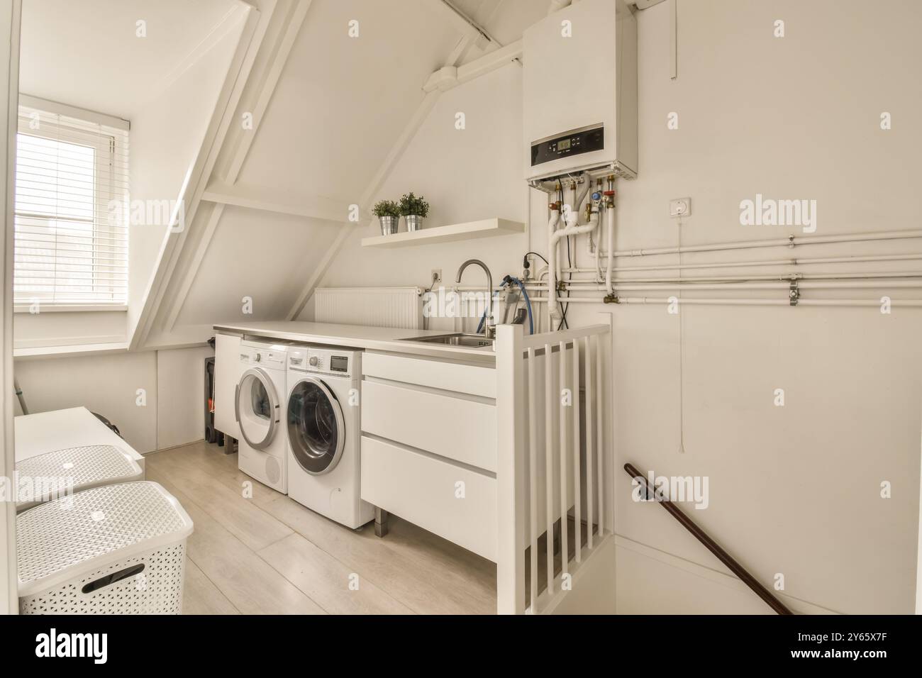 Bright and contemporary attic laundry room with white appliances, wood flooring, and smart use ...