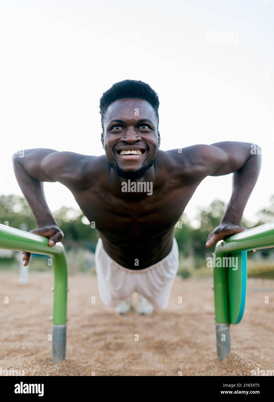 A cheerful man exercises using parallel bars at an outdoor park ...