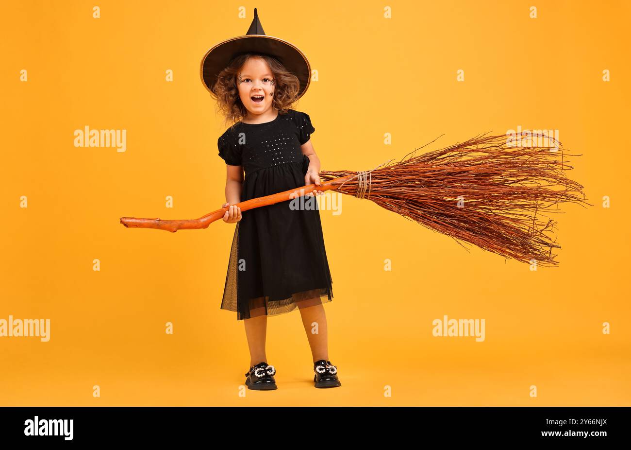 Funny girl with broom dressed like witch on yellow background ...