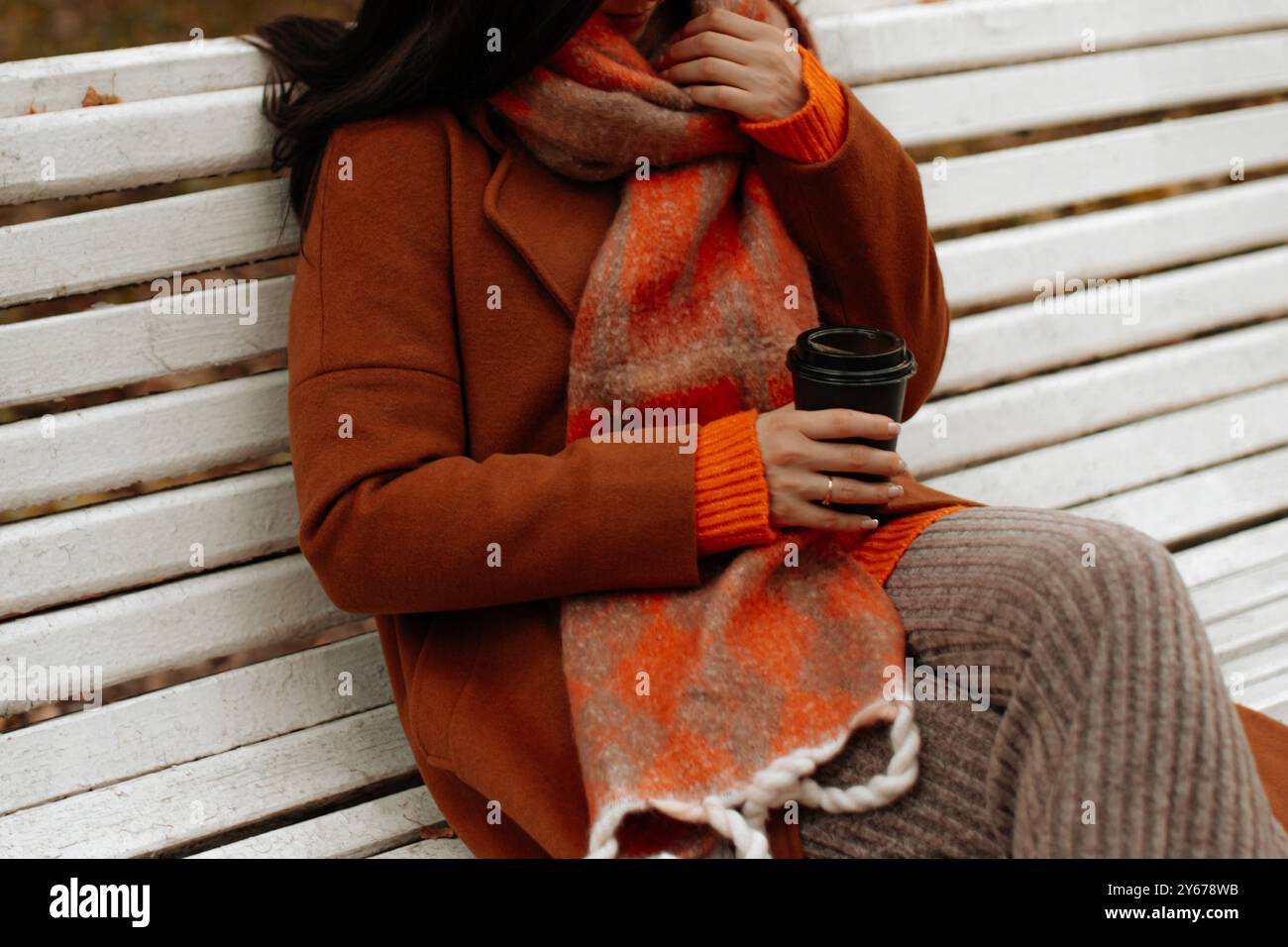 Woman dressed in warm brown coat, pants and orange scarf sitting alone ...