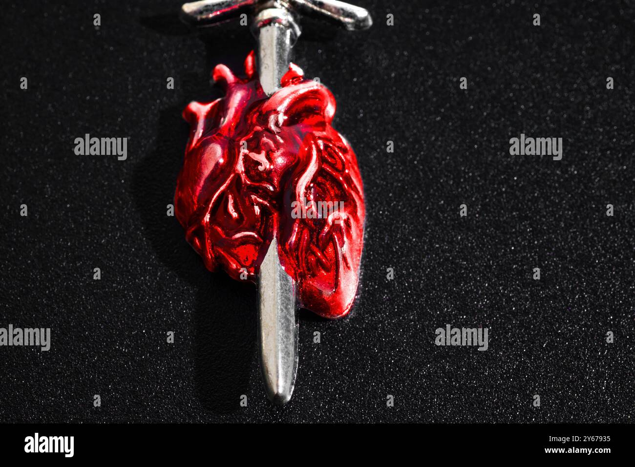 Sword piercing a red anatomical heart against a black surface. Betrayal ...