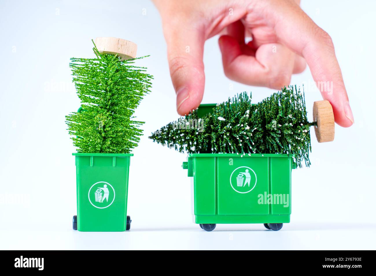Hand placing an artificial Christmas tree into a green trash bin ...