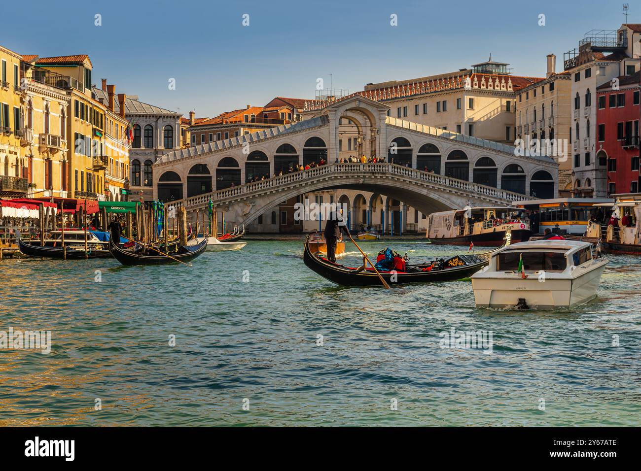 A gondolier steers his gondola along the Grand Canal busy with various ...