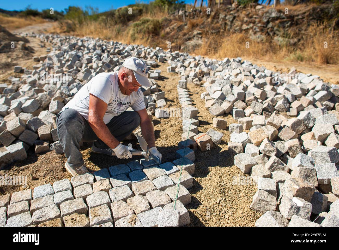 Hard work, man crouched down buiding a cobbled road, the traditional ...