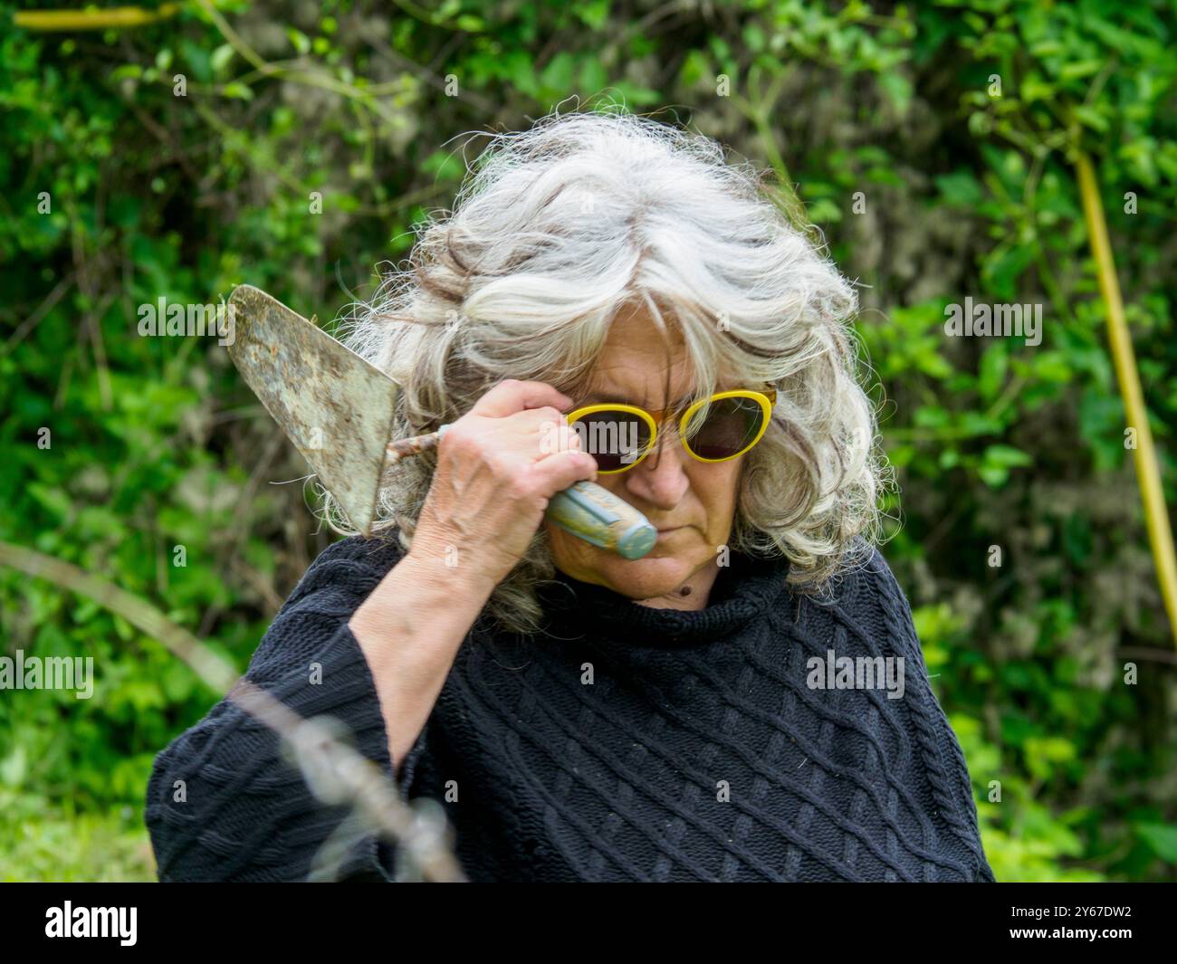Senior woman takes a break from gardening, holding her trowel and ...