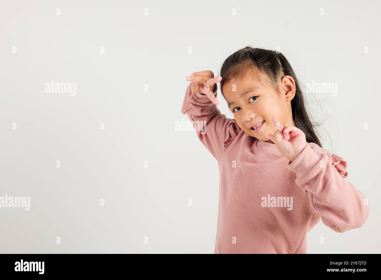 Asian young kid girl showcases optimism and peace by gesturing victory ...
