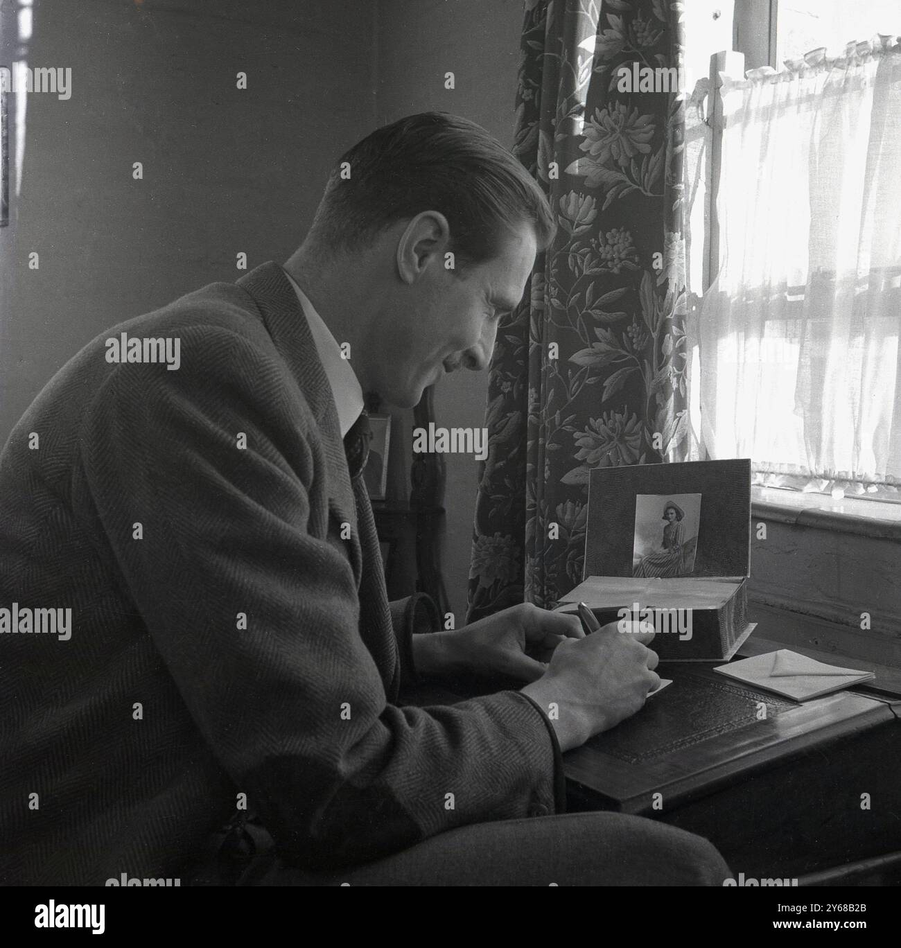1950s, historical, man sitting by a window at a small writing desk ...