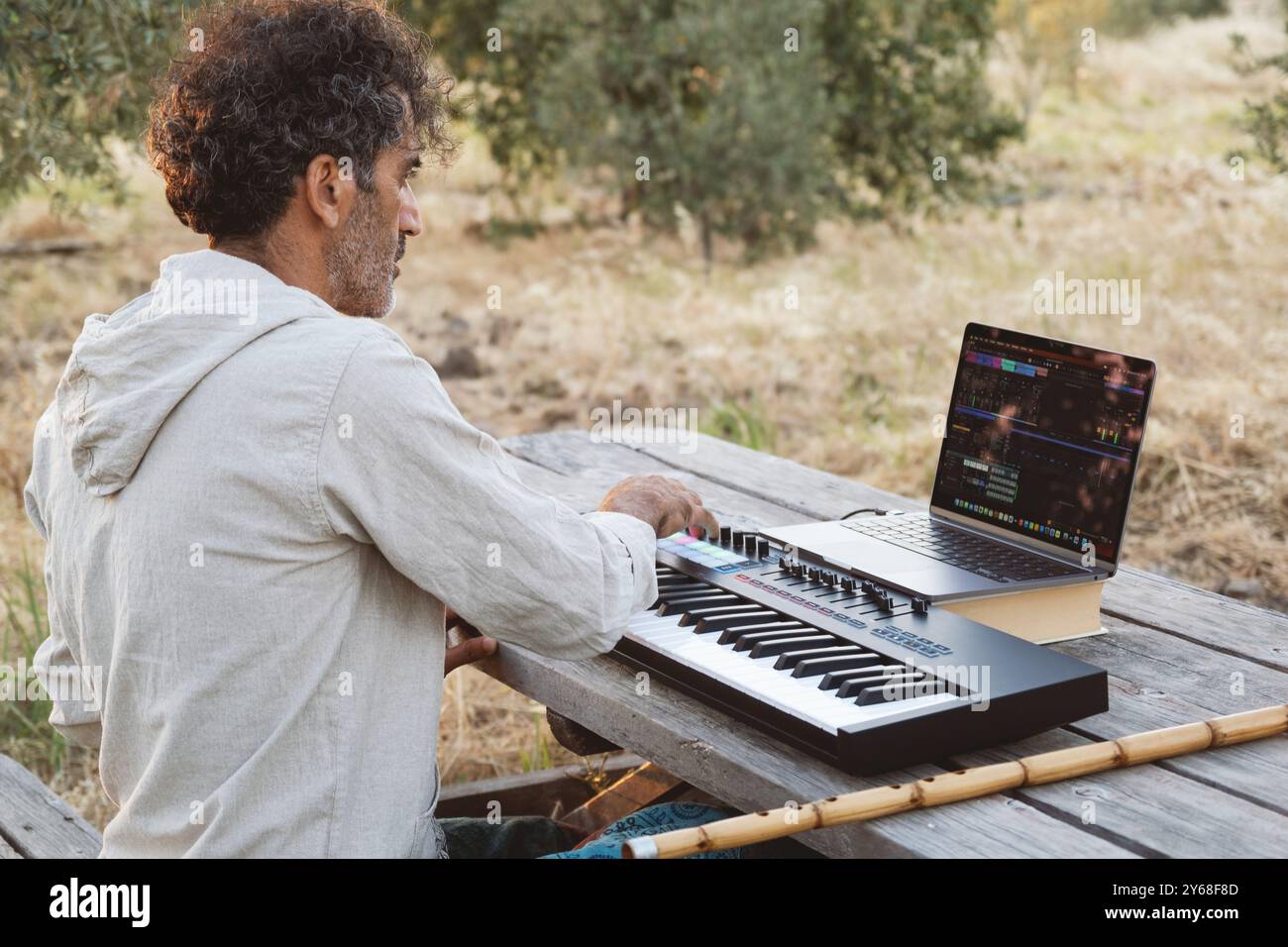 A musician in an olive grove creates music using a keyboard and laptop ...