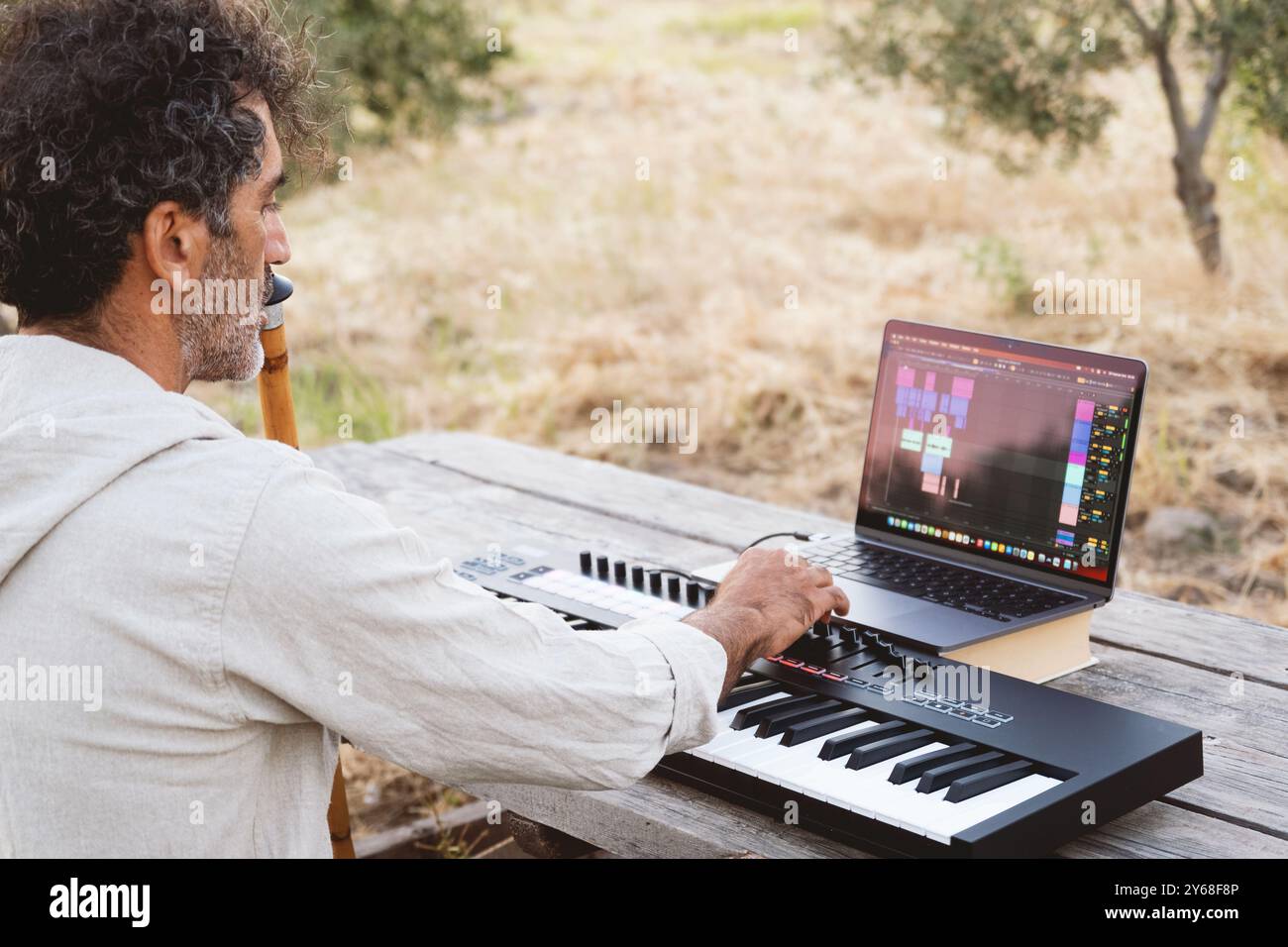 A musician in an olive grove creates music using a keyboard and laptop ...