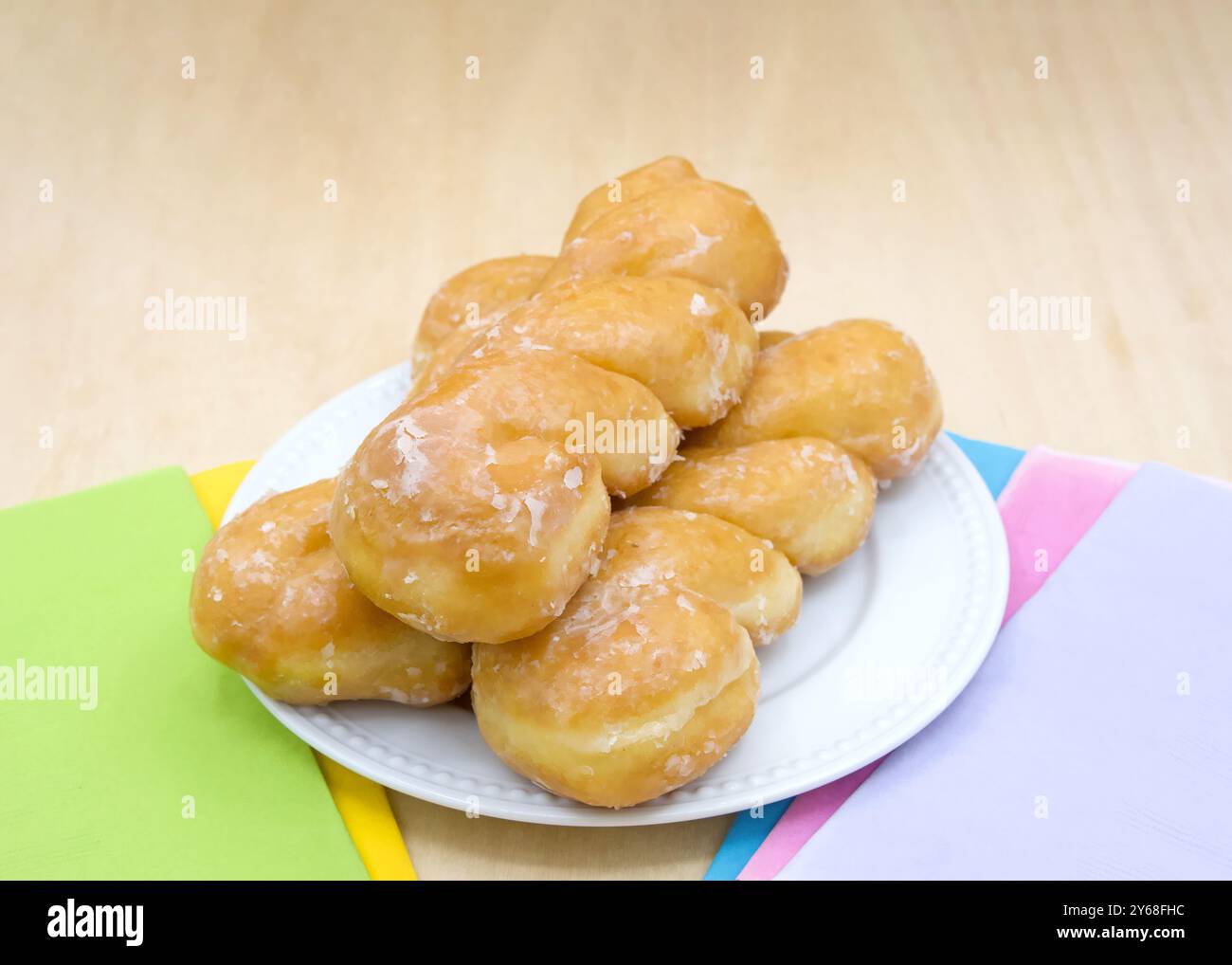 White porcelain plate with glazed twist donuts on a light wood table ...