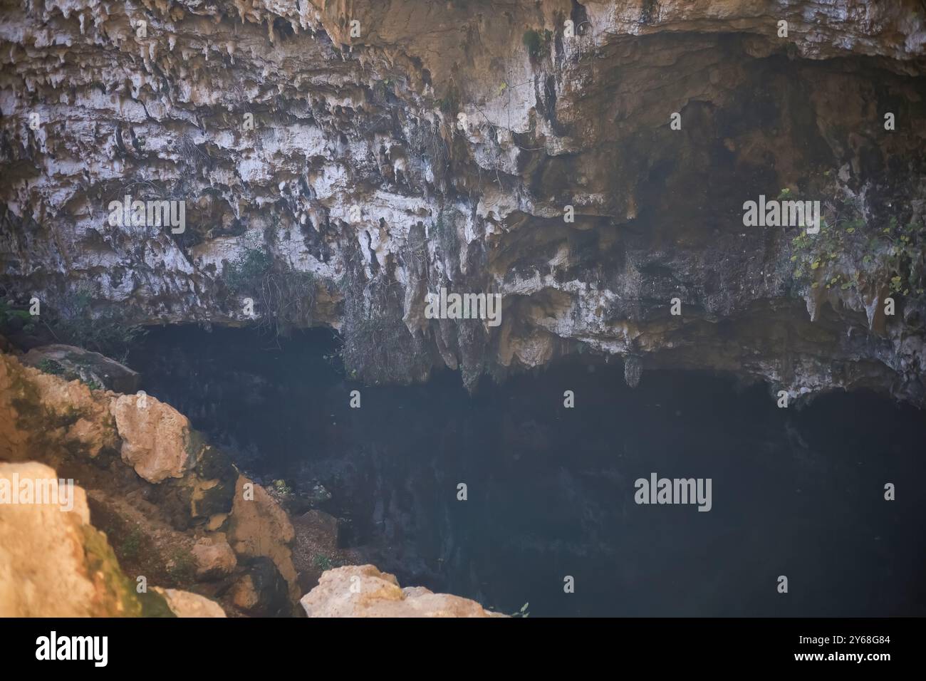 A dark cave entrance surrounded by rocky formations, with still dark ...