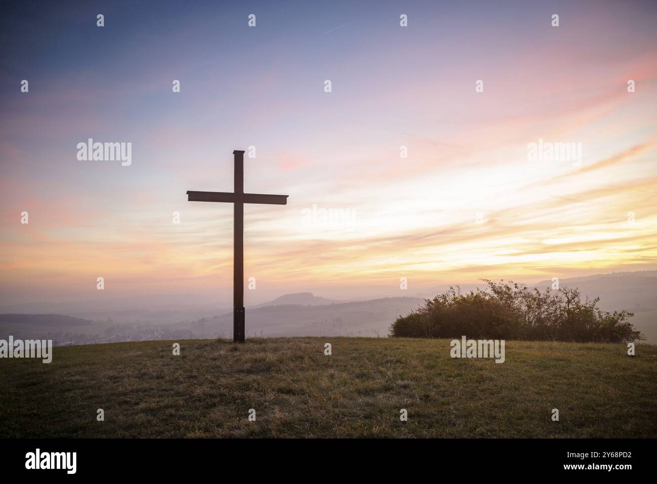 A cross in front of a wide horizon and a colourful sunset sky in a ...