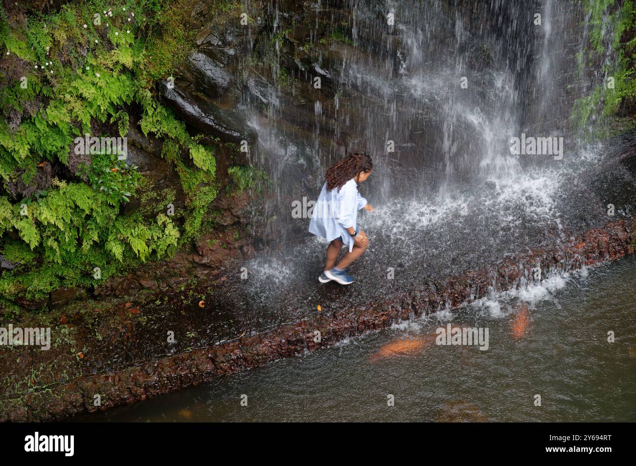 Woman passing beneath a waterfall in monte palace gardens, surrounded ...