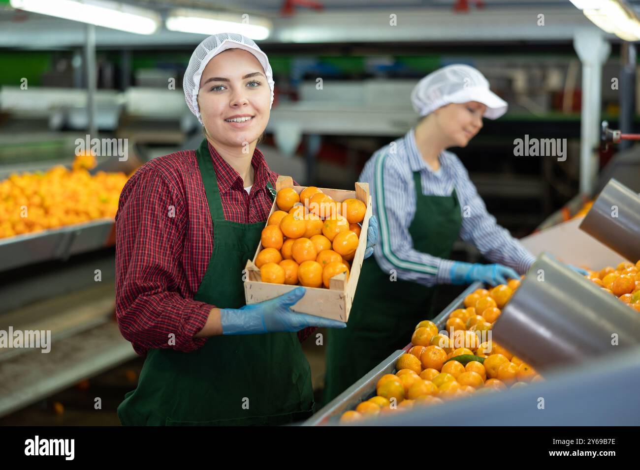 Glad positive female employee in colored uniforms hold a box of fresh ...