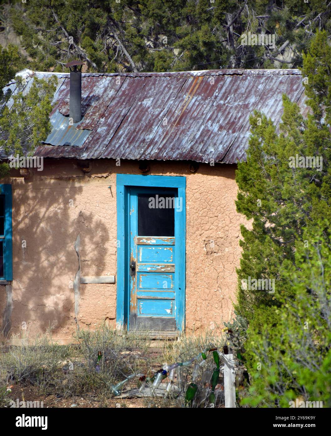 Broken down bottle fence lays in yard of an adobe home, complete with ...