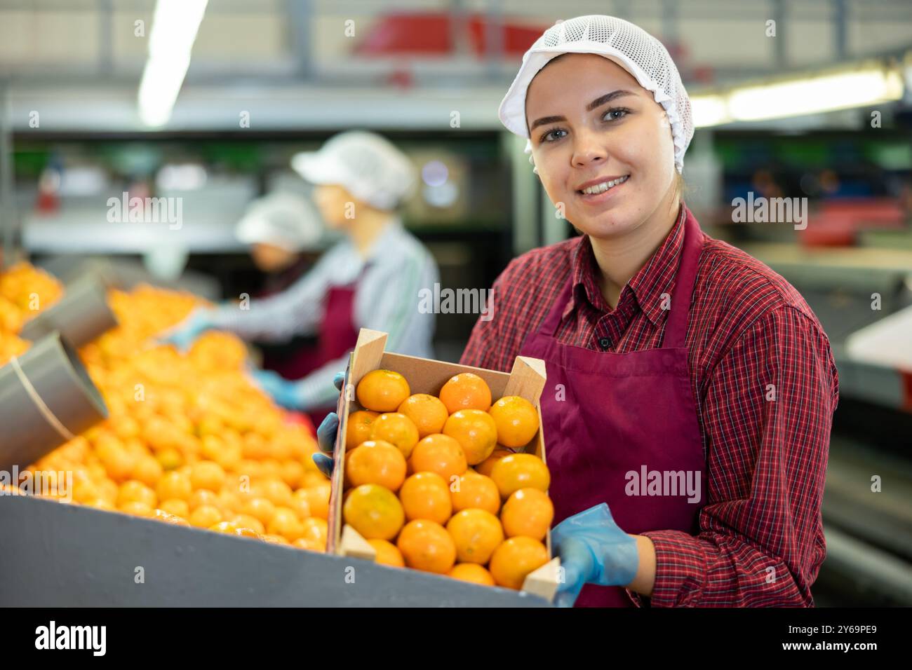 Glad positive female employee in colored uniforms hold a box of fresh ...
