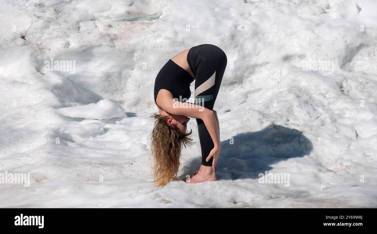 female person practicing yoga outdoors in snow, performing the Standing ...