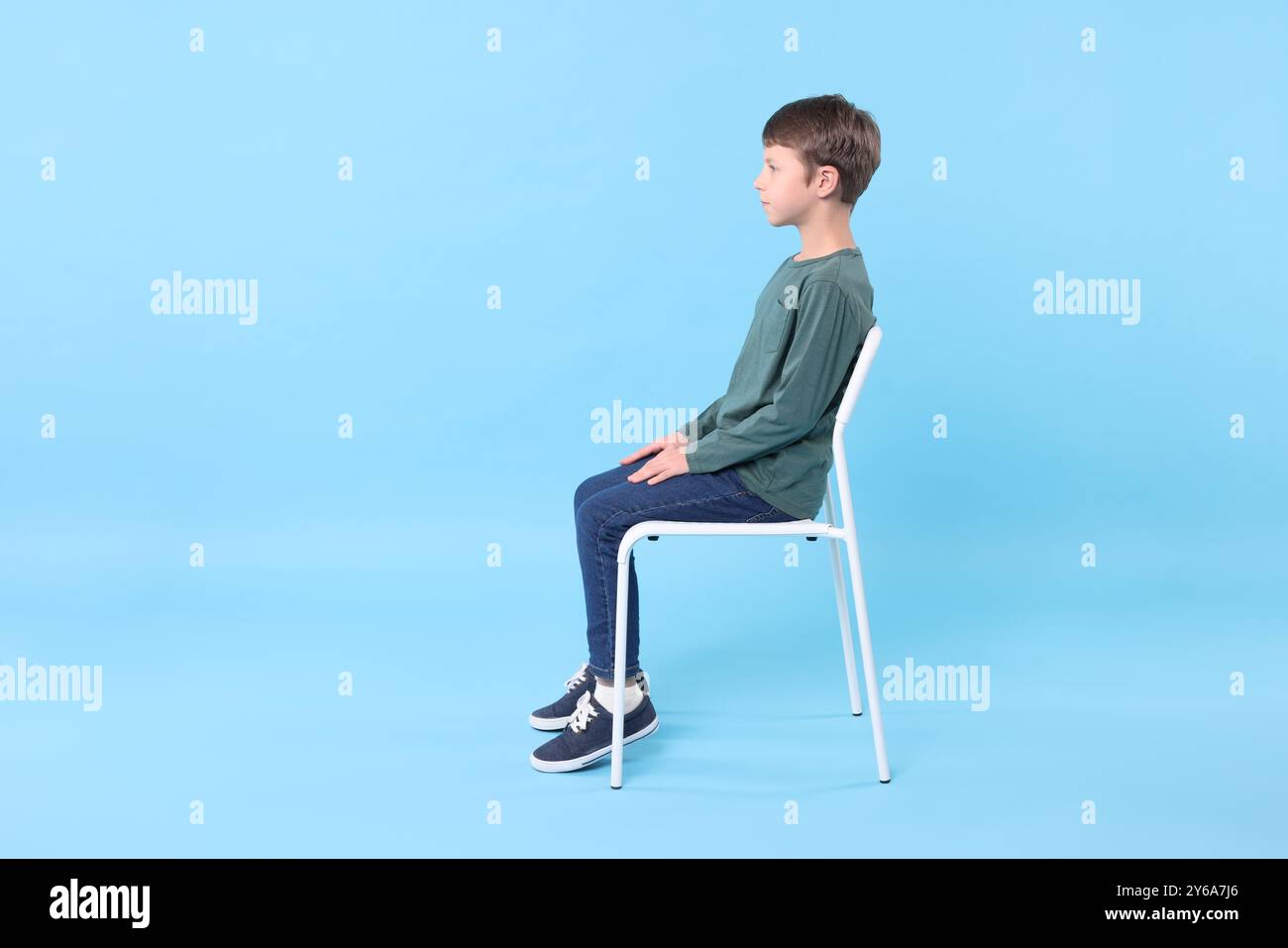 Boy with correct posture sitting on chair against light blue background ...