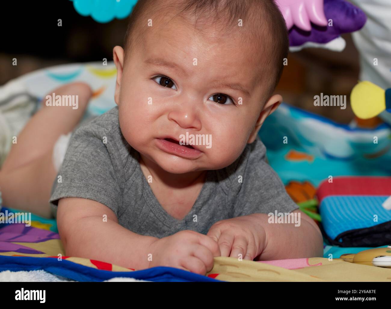 Close up of a cute six month old baby boy laying on his stomach looking ...
