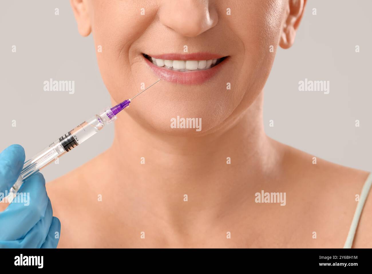 Mature woman receiving filler injection on light background Stock Photo ...