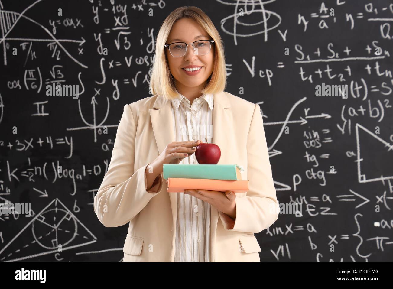 Mature female math teacher with apple and books near blackboard in ...