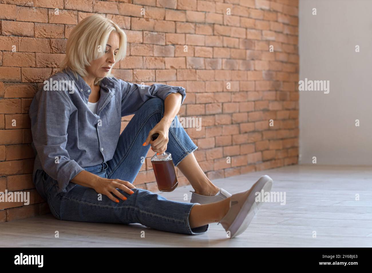 Drunk mature woman with whiskey sitting near brick wall. Concept of ...