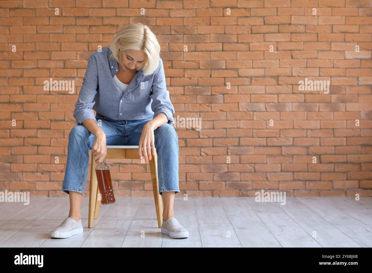 Drunk mature woman with whiskey sitting on chair near brick wall ...