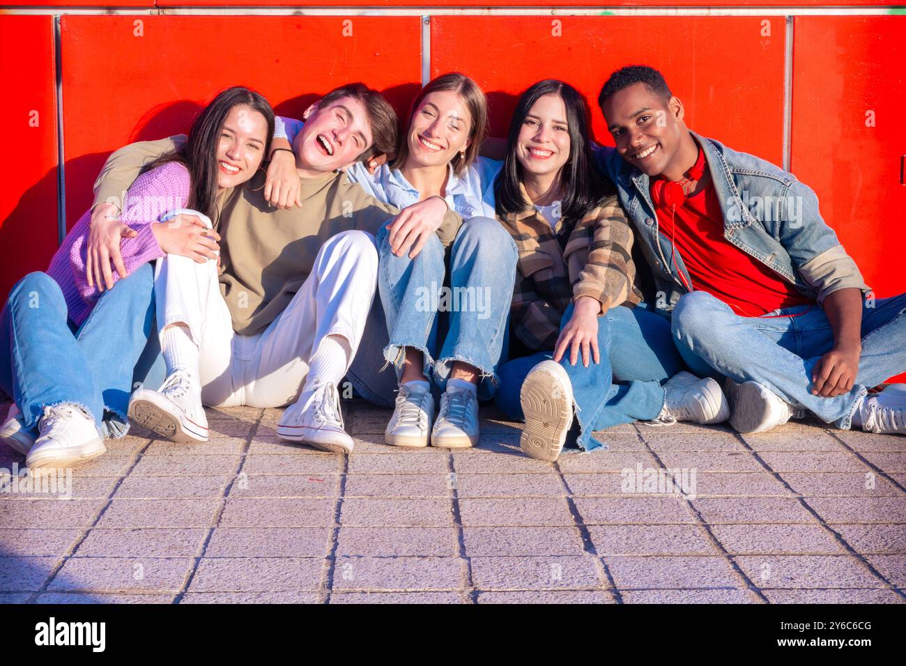 Teenagers sitting on the floor hugging each other on a red background ...