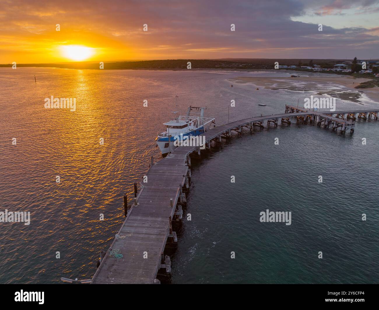 Aerial view of fishing boat alongside a curved jetty under a glowing ...