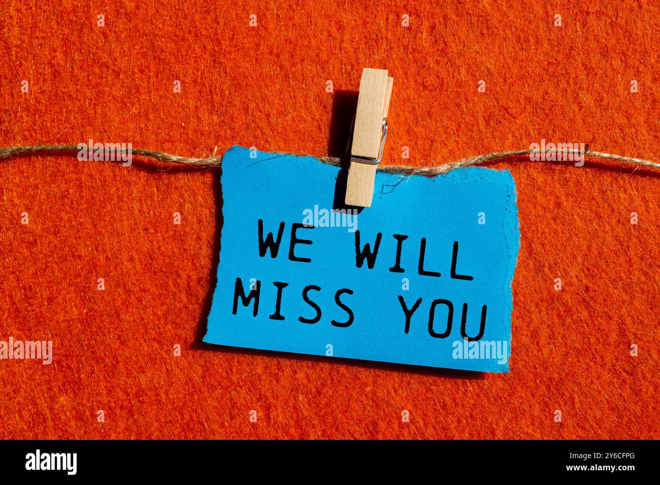 We will miss you message written on ripped blue torn paper piece on orange background ...