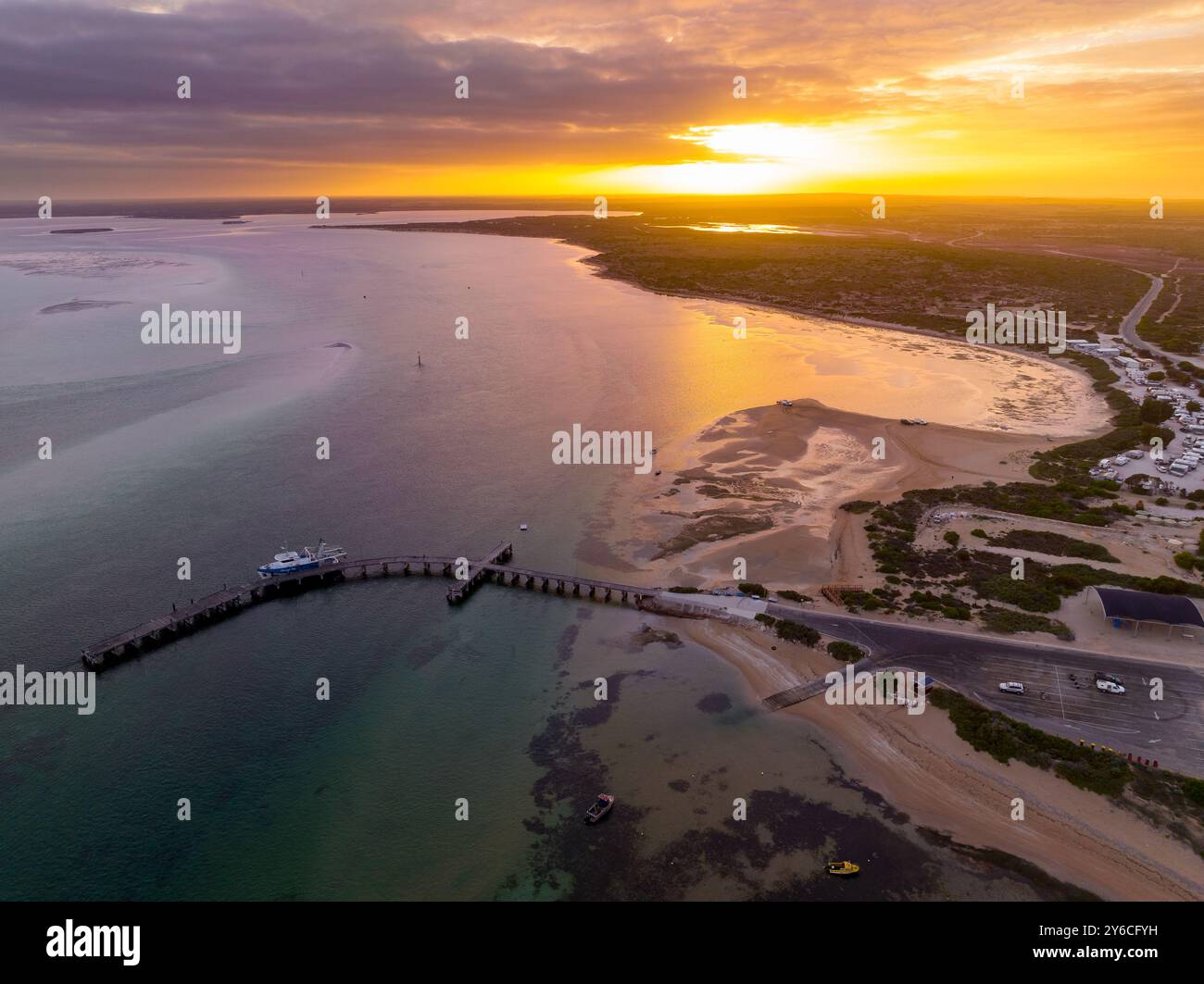 Aerial view of fishing boat alongside a curved jetty under a glowing ...