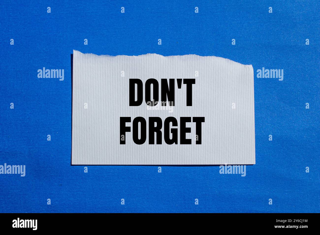 Don't forget message written on ripped white torn paper piece with blue background. Conceptual ...