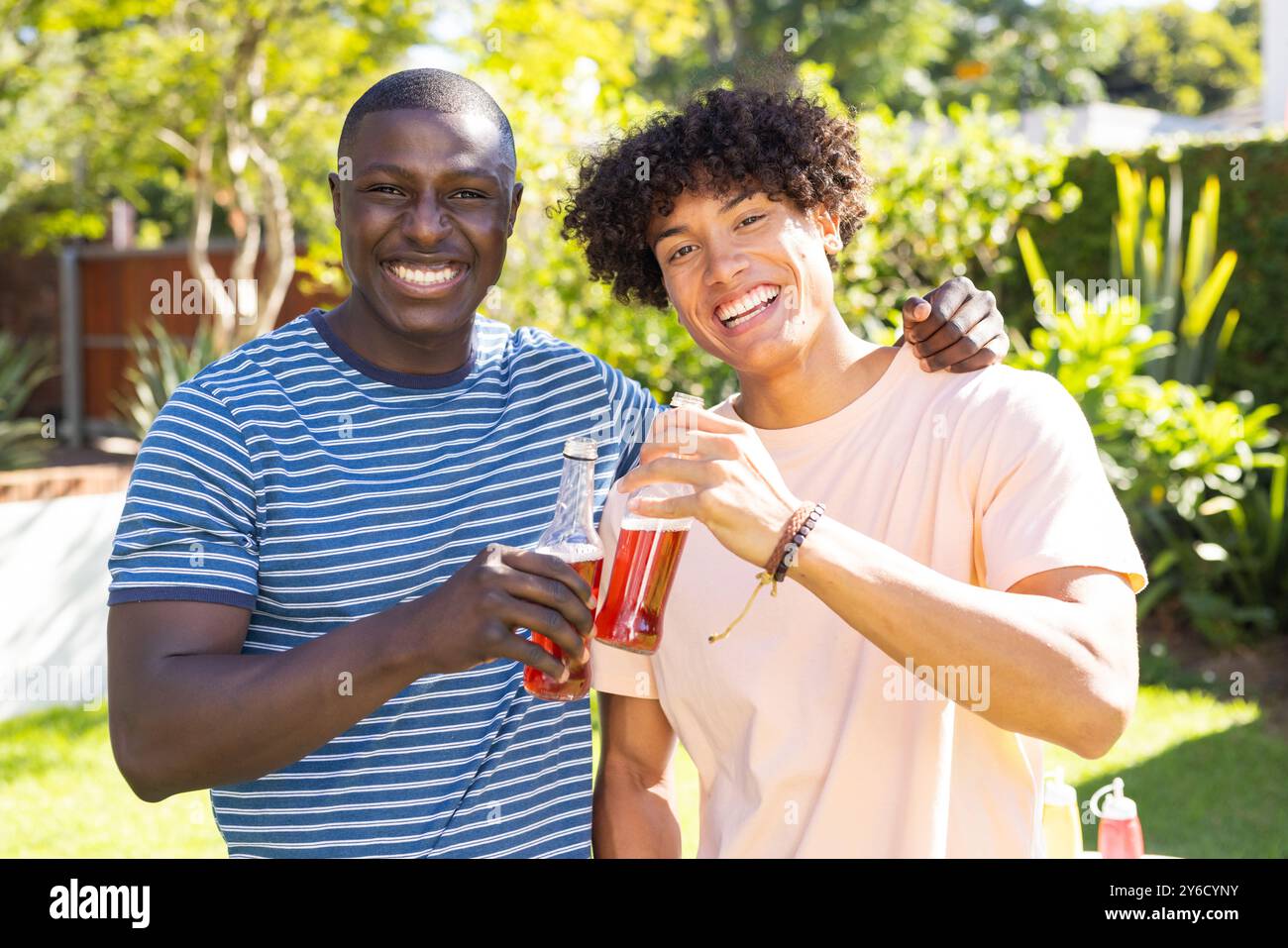 Holding soda bottles, smiling two diverse male friends enjoying outdoor ...