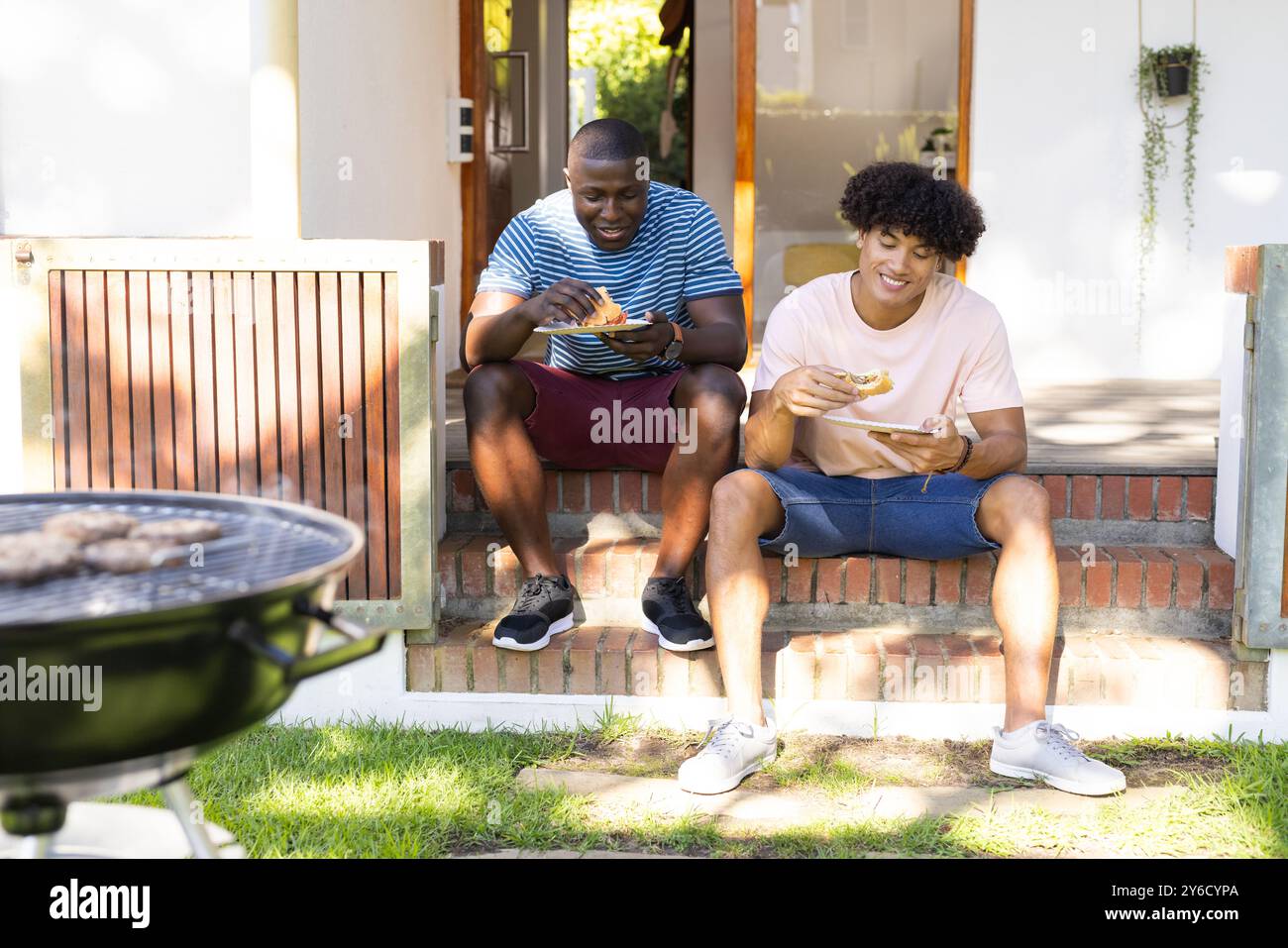Eating burgers and relaxing, two diverse male friends enjoying outdoor ...