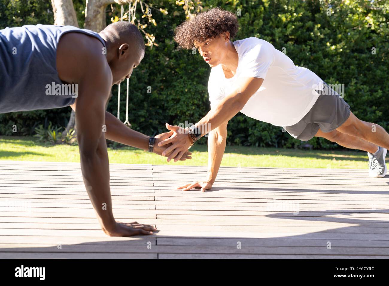 Doing push-ups, two diverse male friends shaking hands outdoors ...