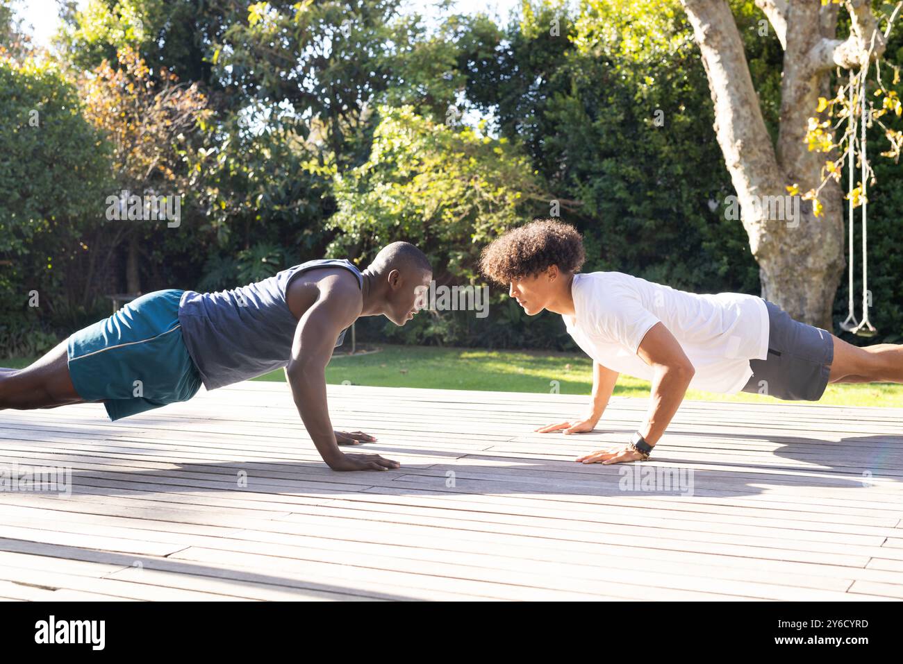 Exercising outdoors, two diverse male friends doing push-ups together ...
