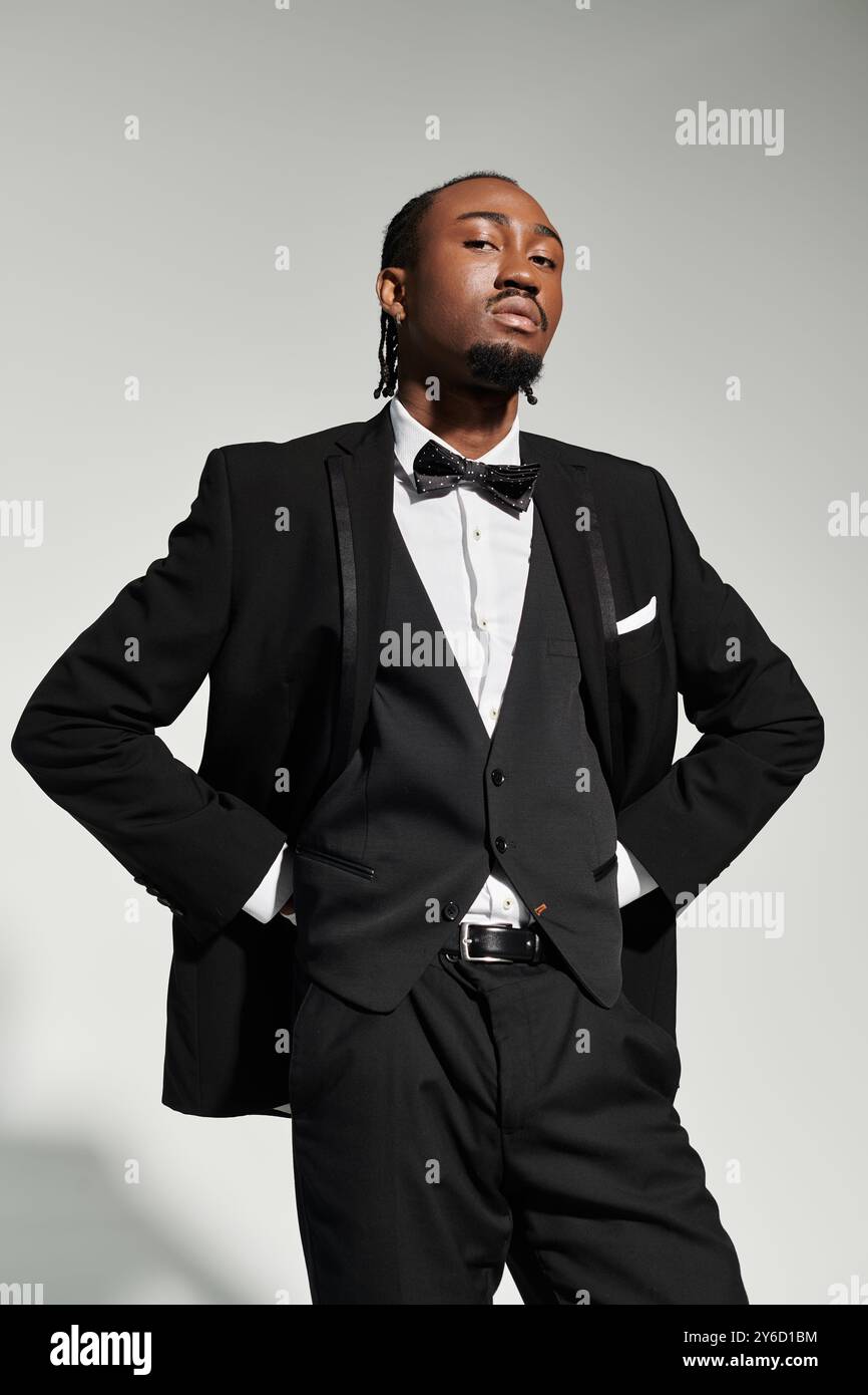 A young man dressed in a sharp suit and vest stands proudly on a grey ...